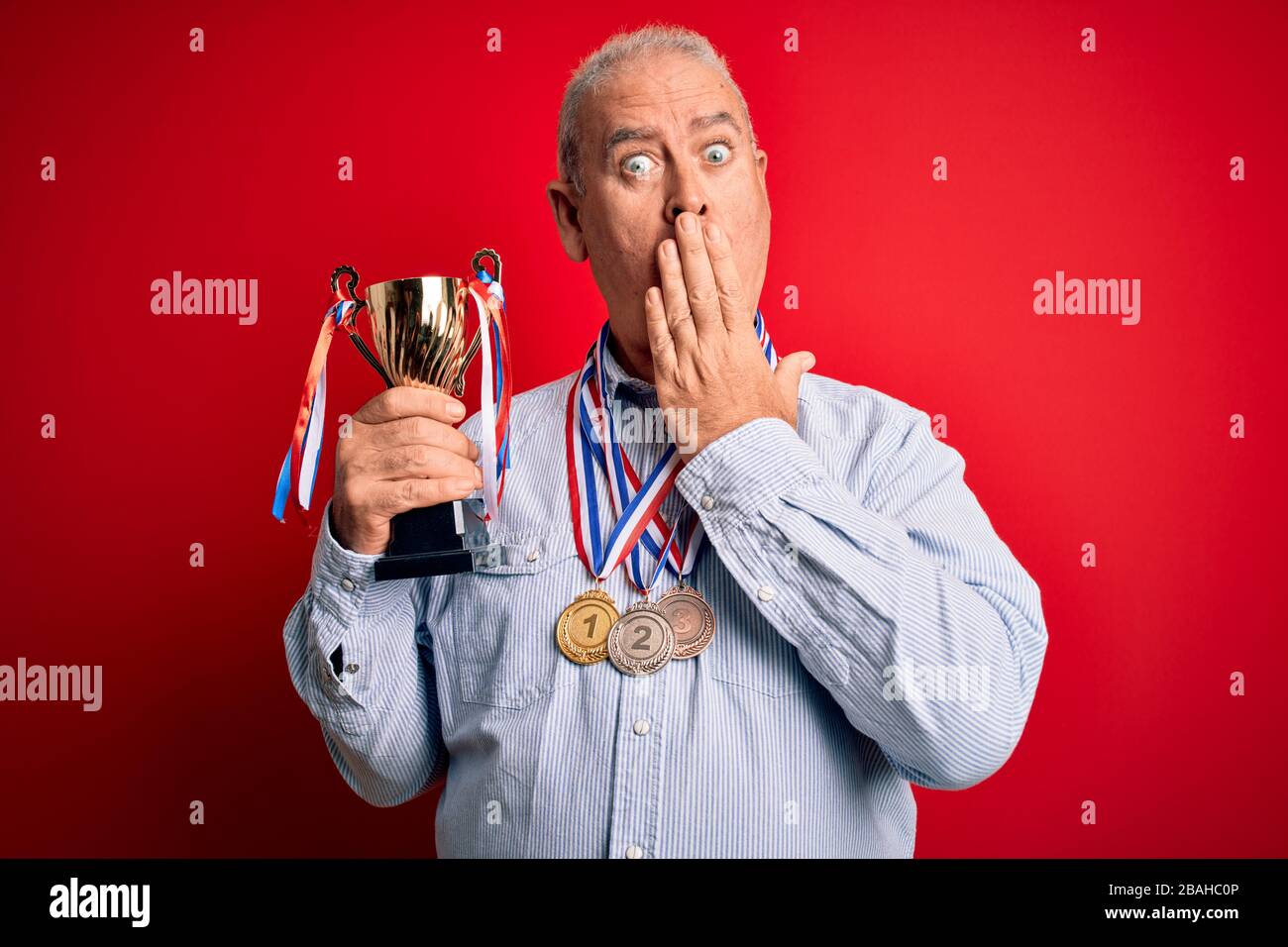 Middle age hoary successful man wearing medals holding trophy over ...
