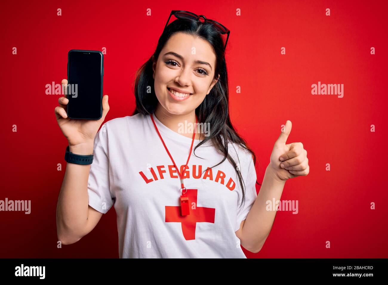 Young lifeguard woman showing smartphone screen over red background ...