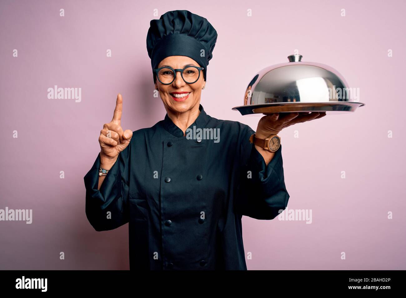 Middle age brunette chef woman wearing cooker uniform and hat holding ...