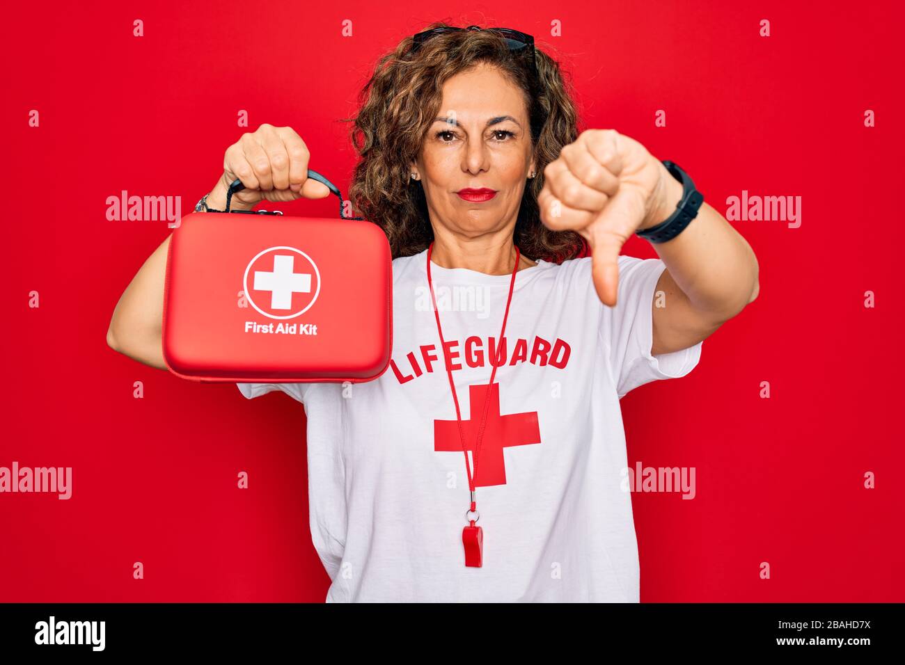 Middle age senior summer lifeguard woman holding first aid kit over red ...