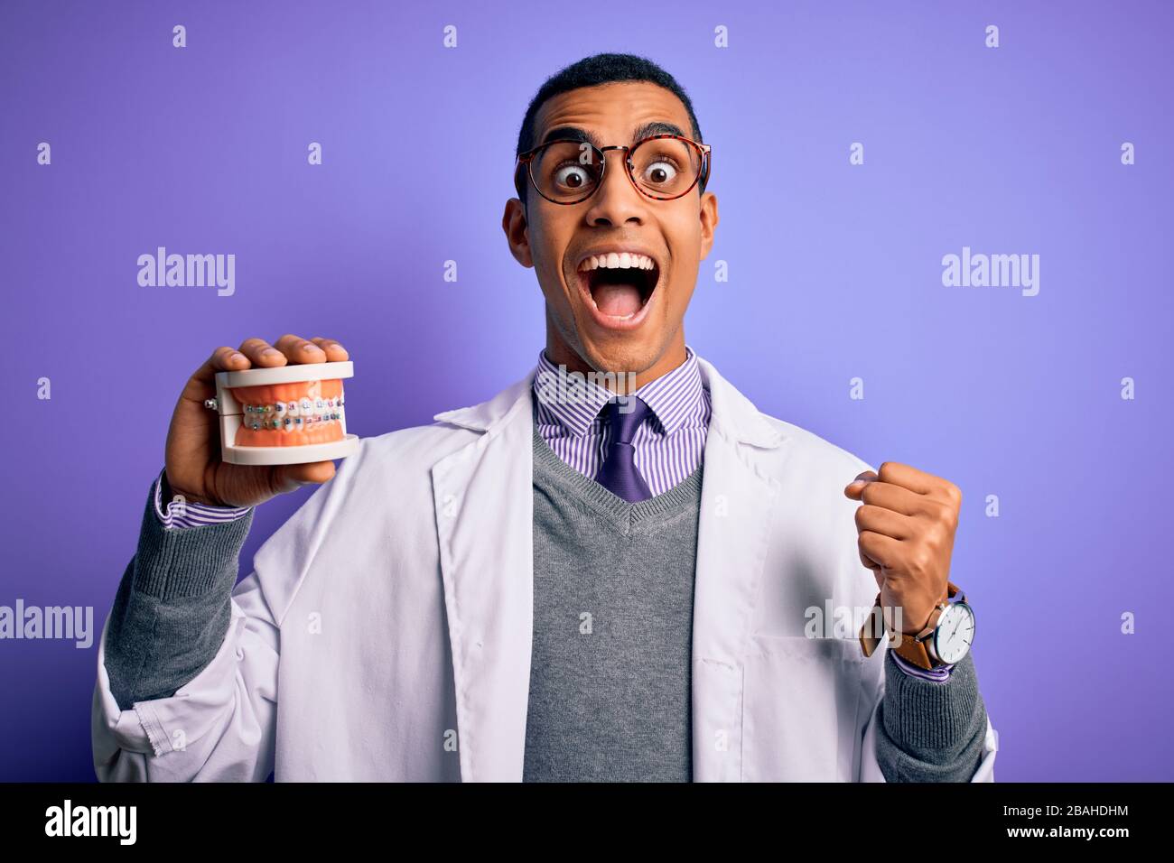 Young handsome african american dentist man holding denture teeth with ...