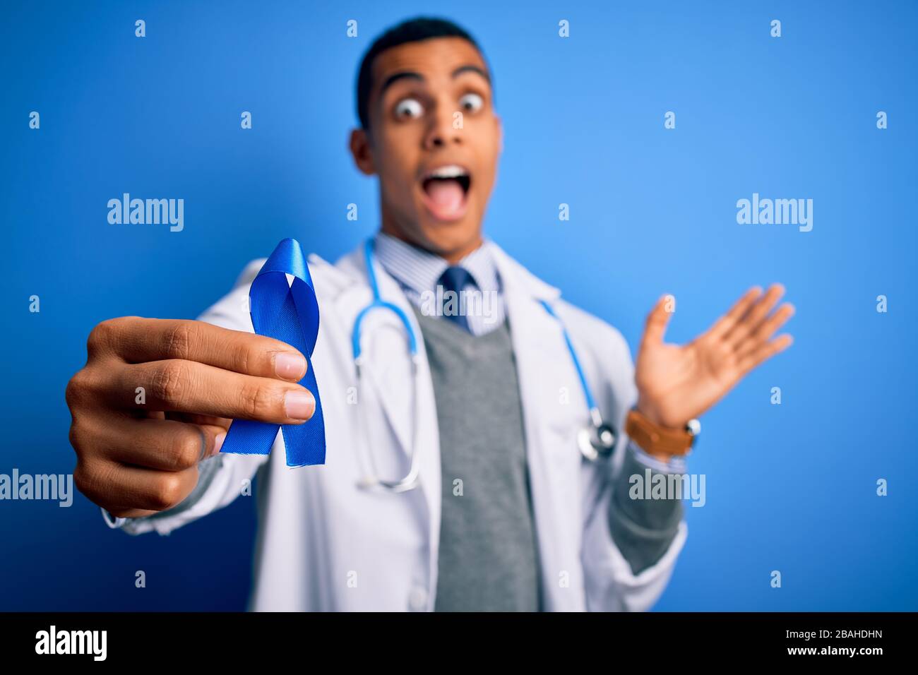 Young handsome african american doctor man holding blue cancer ribbon ...
