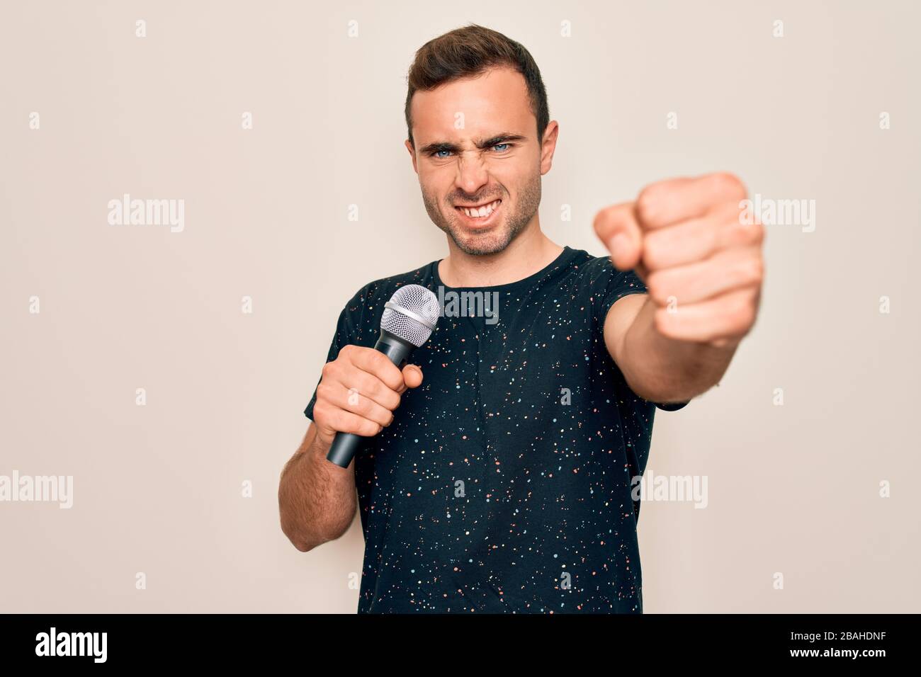 Young handsome singer man with blue eyes singing using microphone over white background annoyed ...