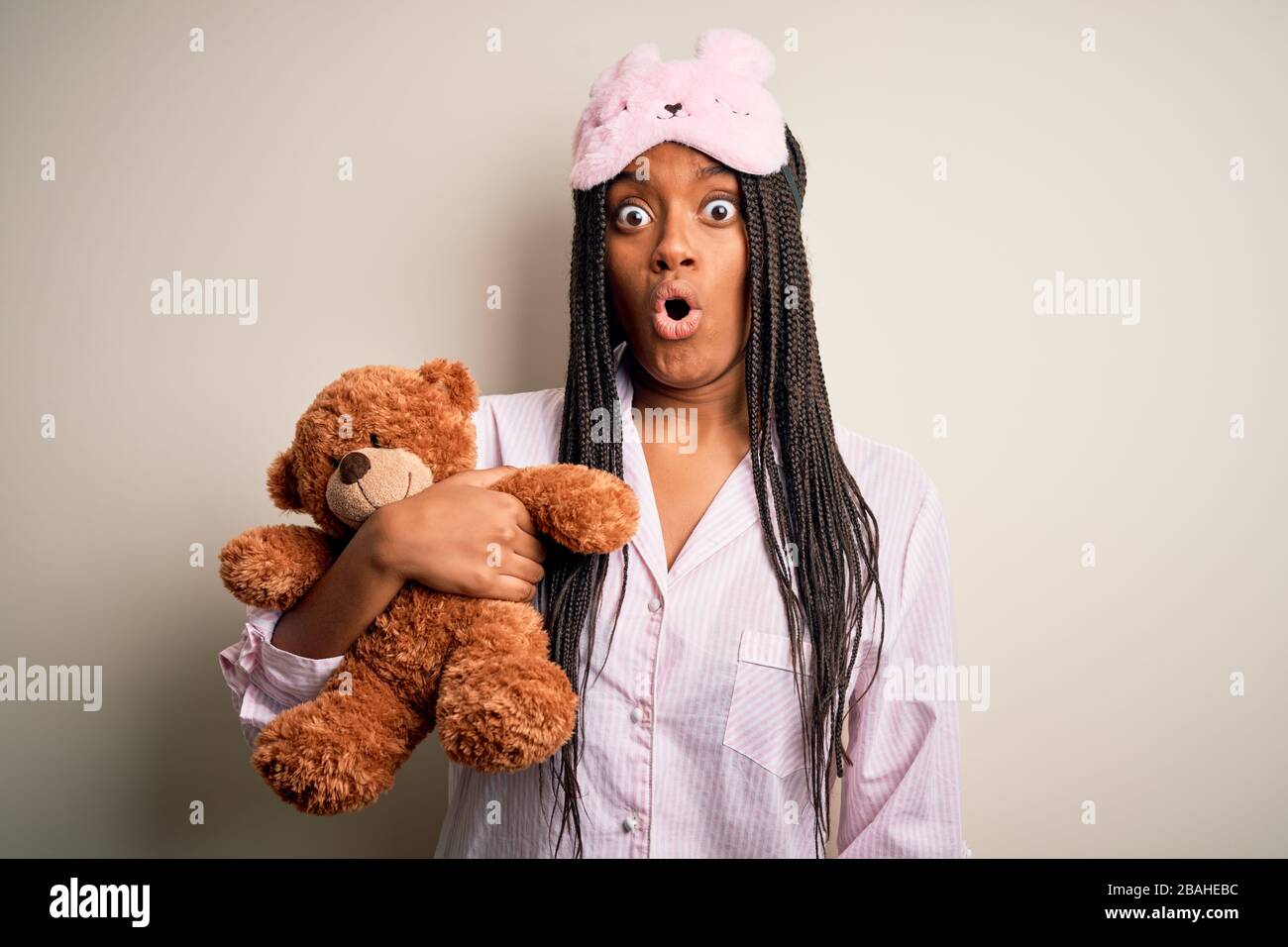 Young african american woman wearing pajama and eye mask hugging teddy ...