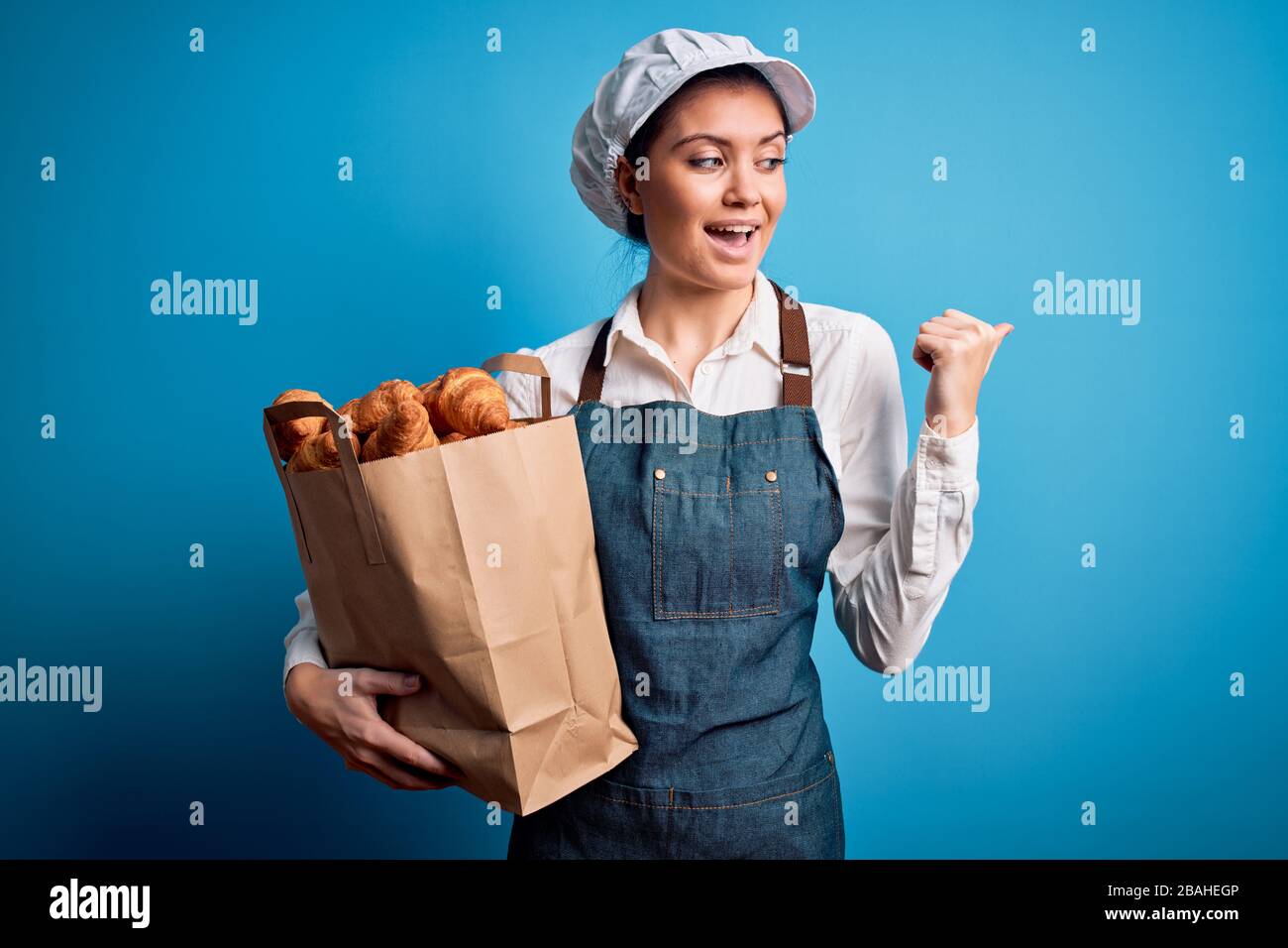 Young beautiful baker woman with blue eyes wearing apron holding paper ...