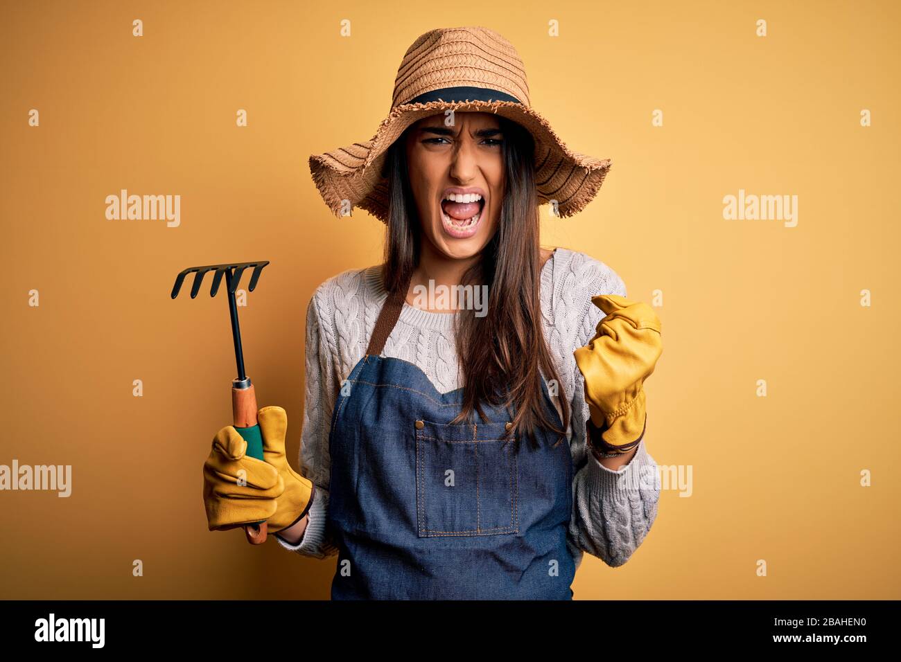 Young beautiful farmer woman wearing apron and hat using rake over ...