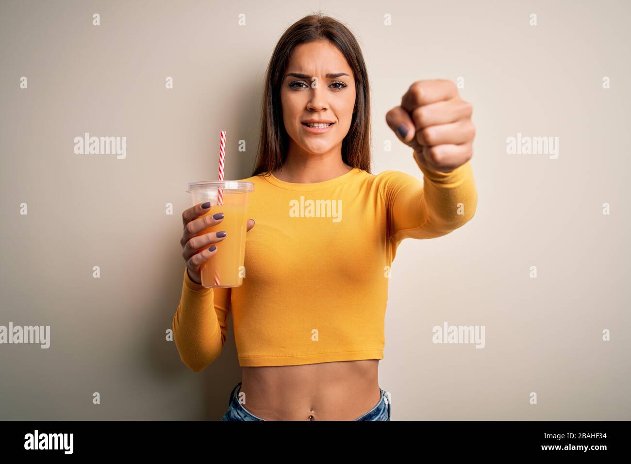 Young beautiful brunette woman drinking healthy orange juice over white ...