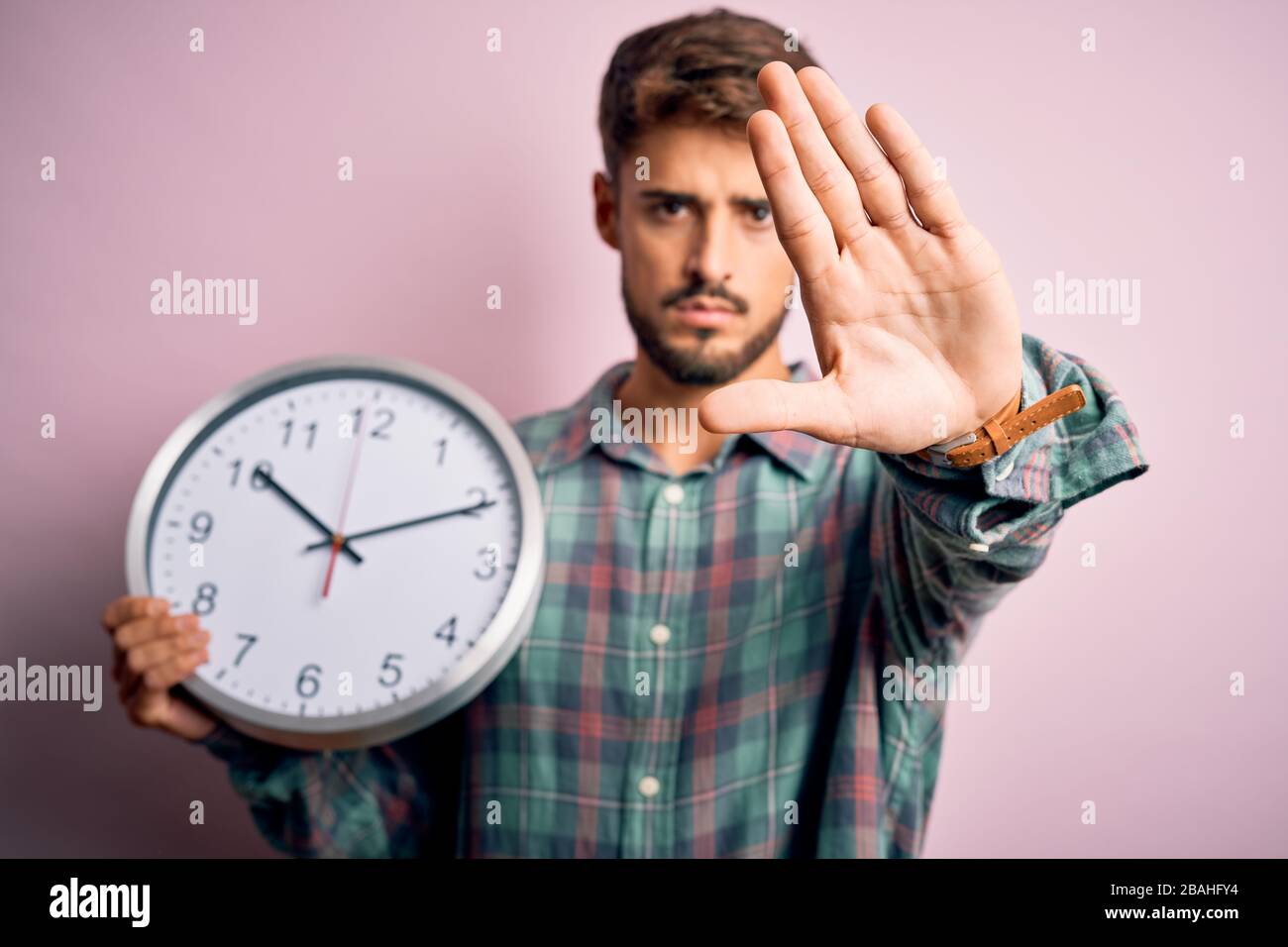 Young man with beard doing countdown using big clock over isolated pink ...