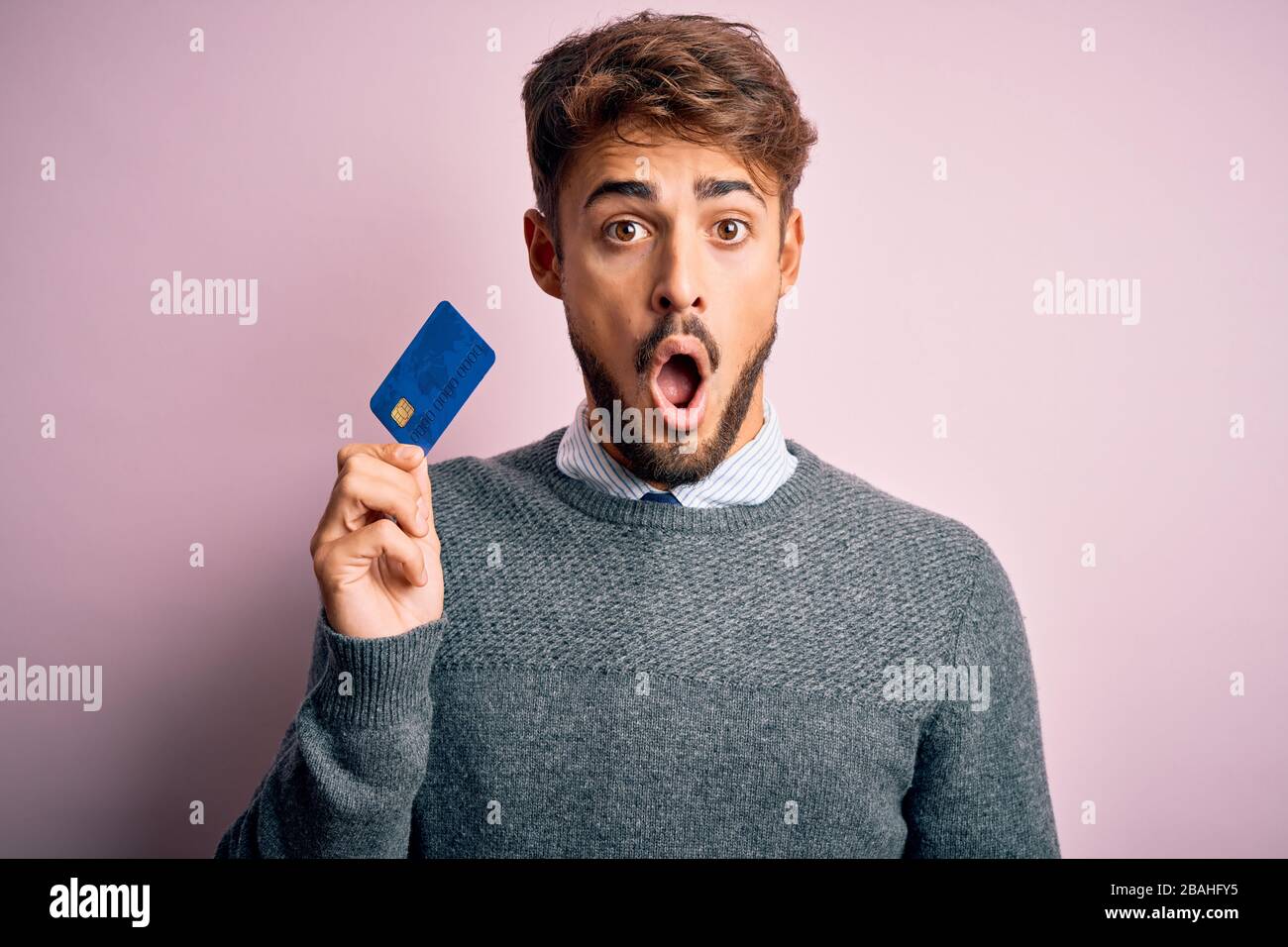 Young customer man with beard holding credit card for payment over pink ...