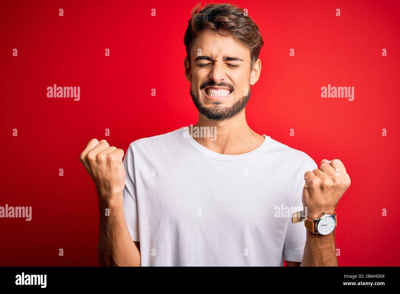 Young handsome man with beard wearing casual t-shirt standing over red ...