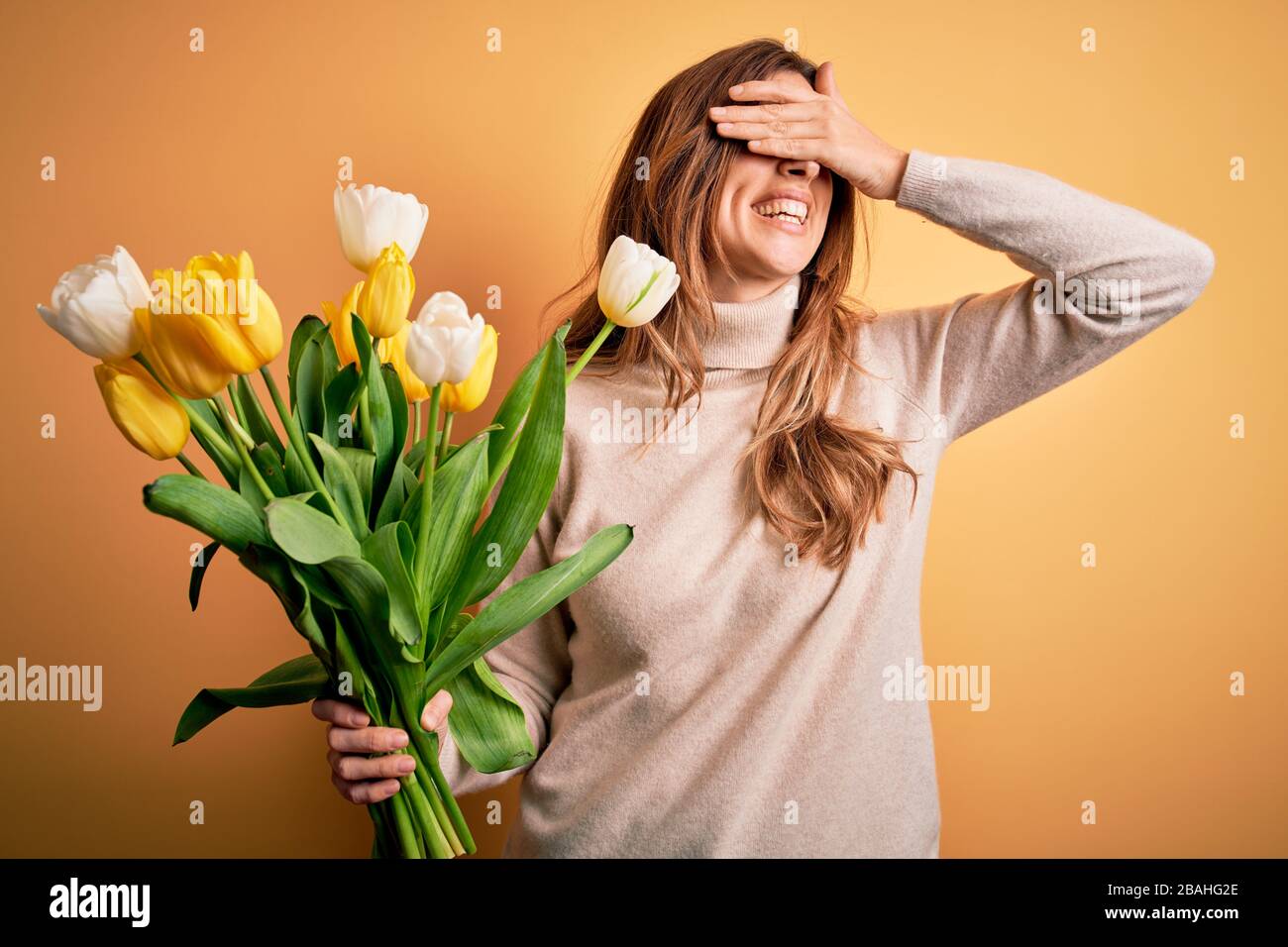 Young beautiful brunette woman holding bouquet of yellow tulips over ...