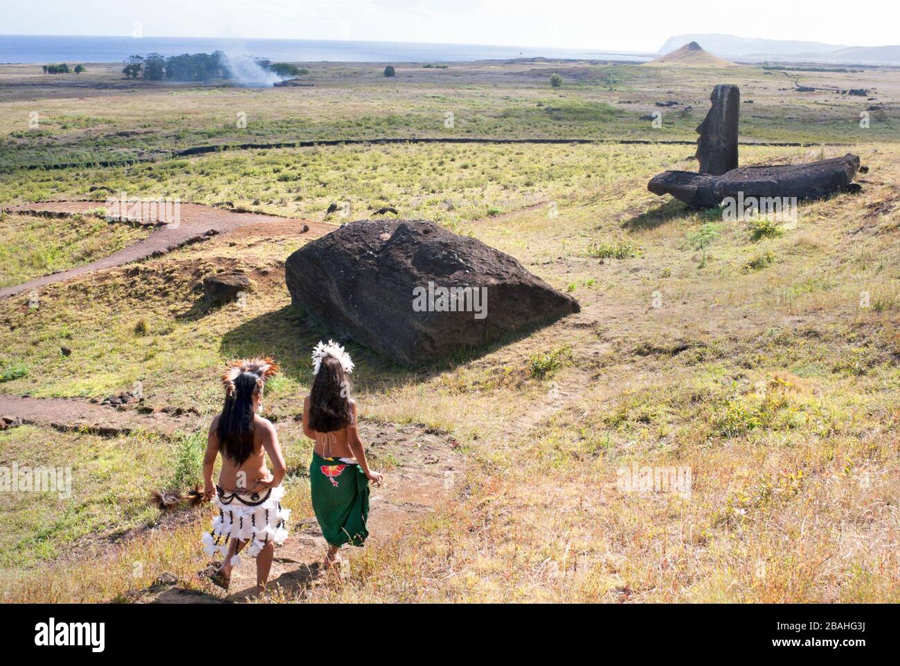 Rapa Nui women, dancers walking along pathway past fallen moai in Rano ...