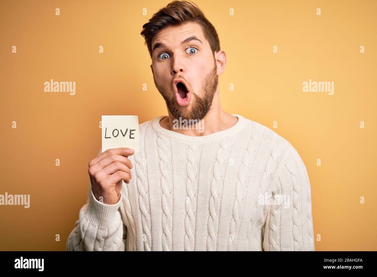 Young blond romantic man with beard and blue eyes holding paper with ...