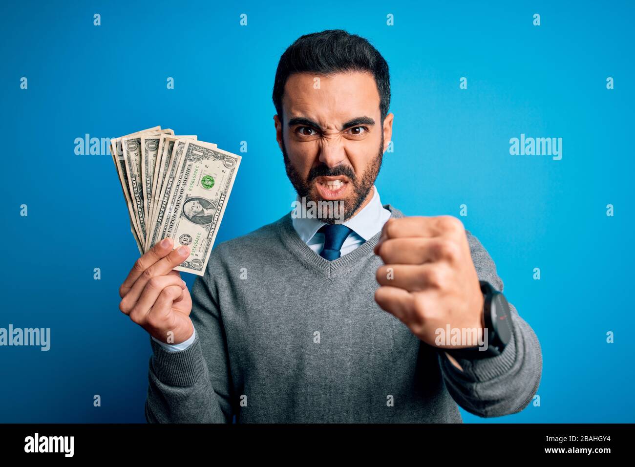 Young handsome man with beard holding bunch of dollars banknotes over ...