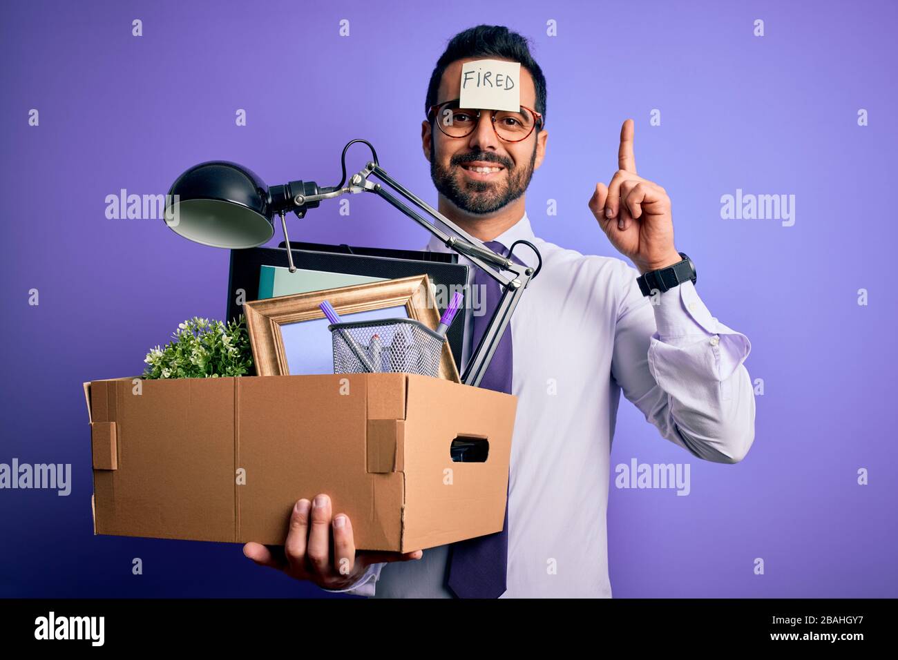 Young handsome businessman with beard holding cardboard box with fired ...