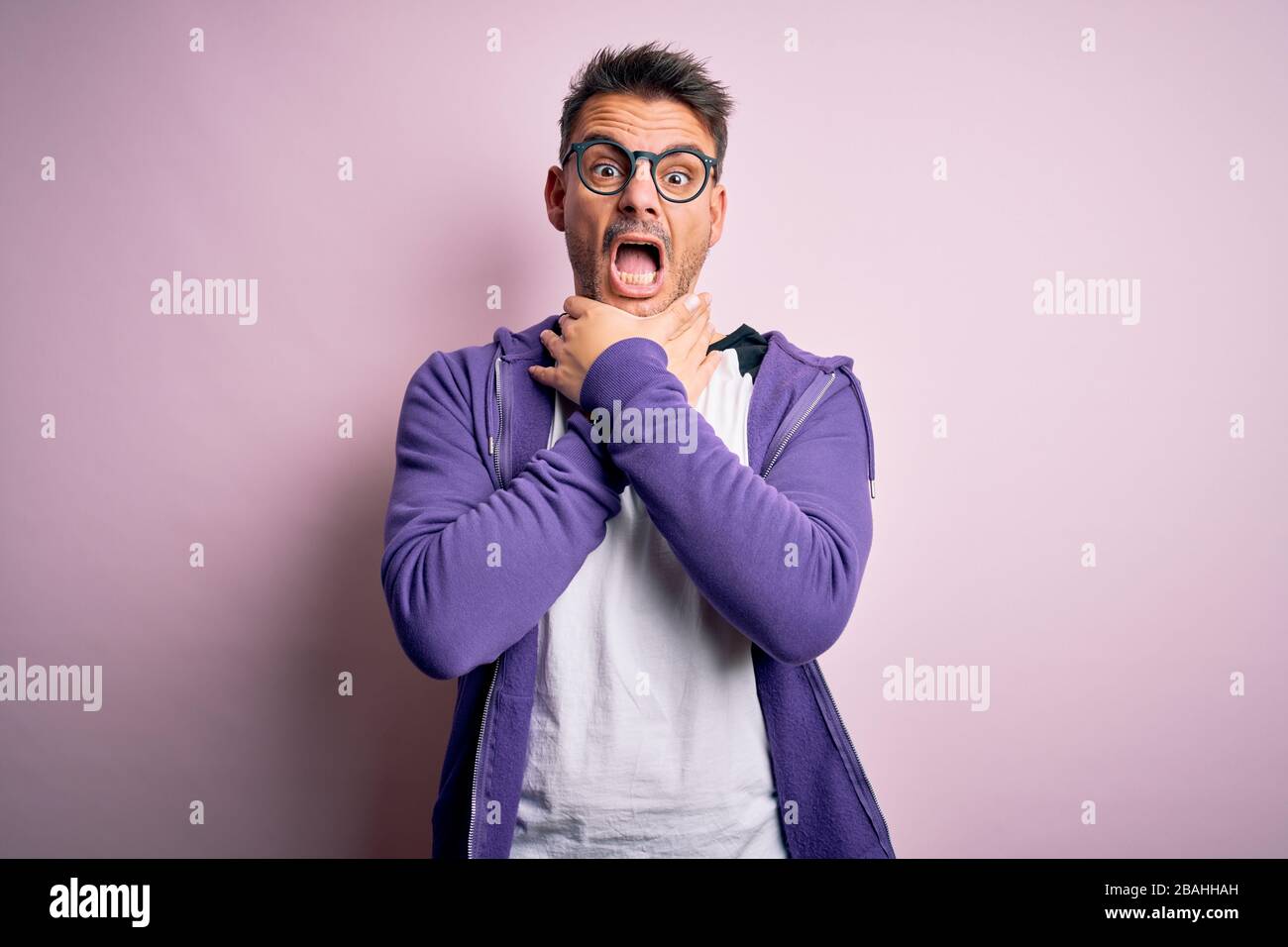 Young handsome man wearing purple sweatshirt and glasses standing over ...