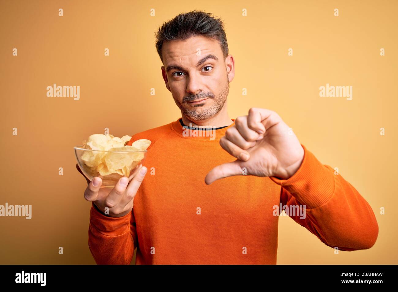 Young handsome man holding bowl with potatoes chips over isolated ...