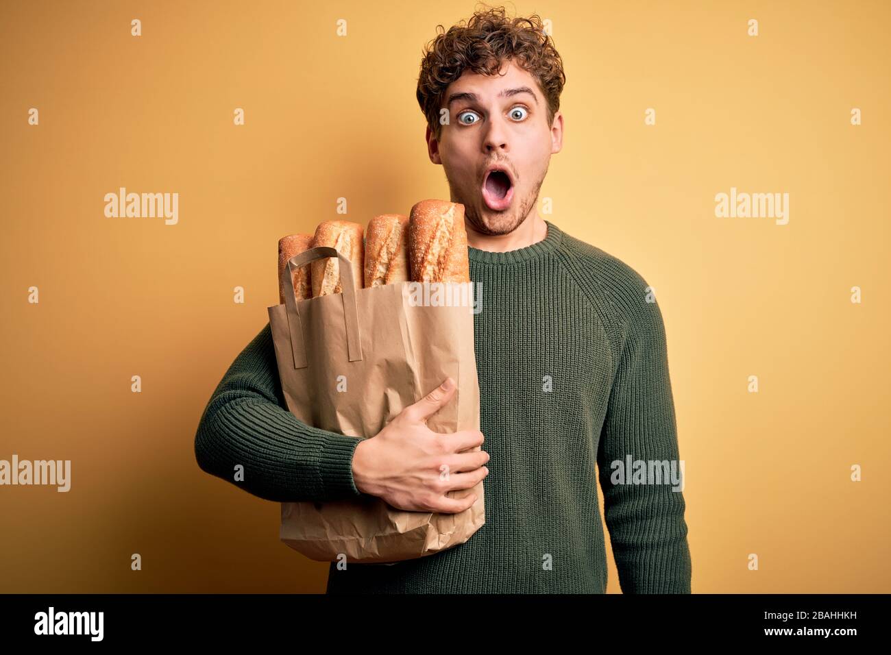 Young blond man with curly hair holding paper bag with bread over ...