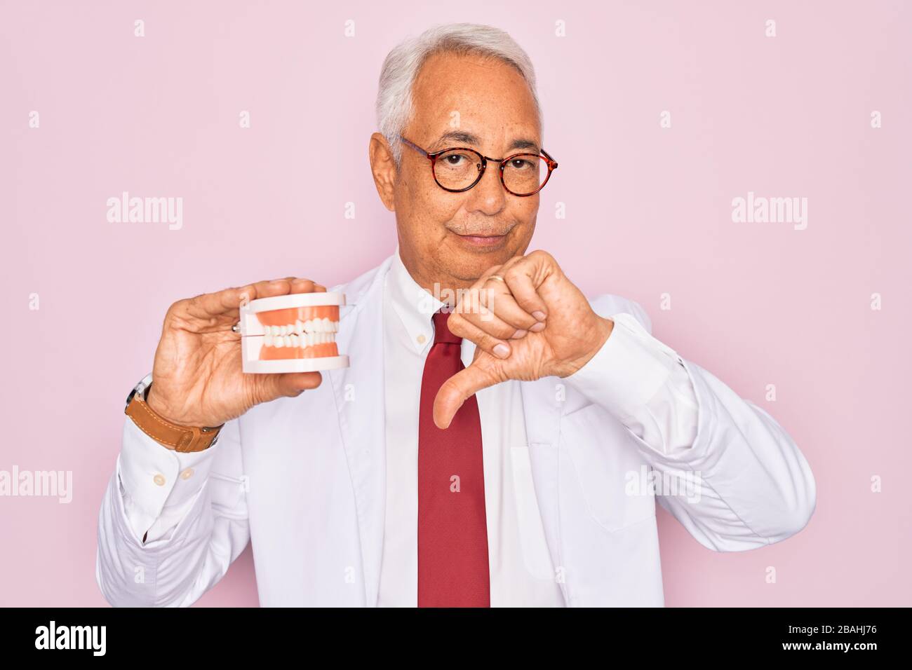 Middle age senior grey-haired dentist man holding prosthesis denture ...
