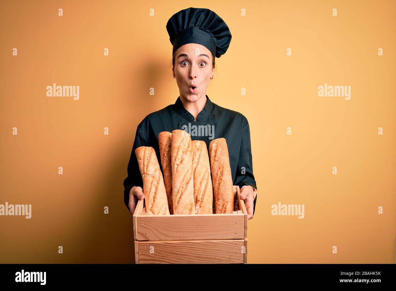 Young beautiful baker woman wearing cooker uniform and hat holding ...