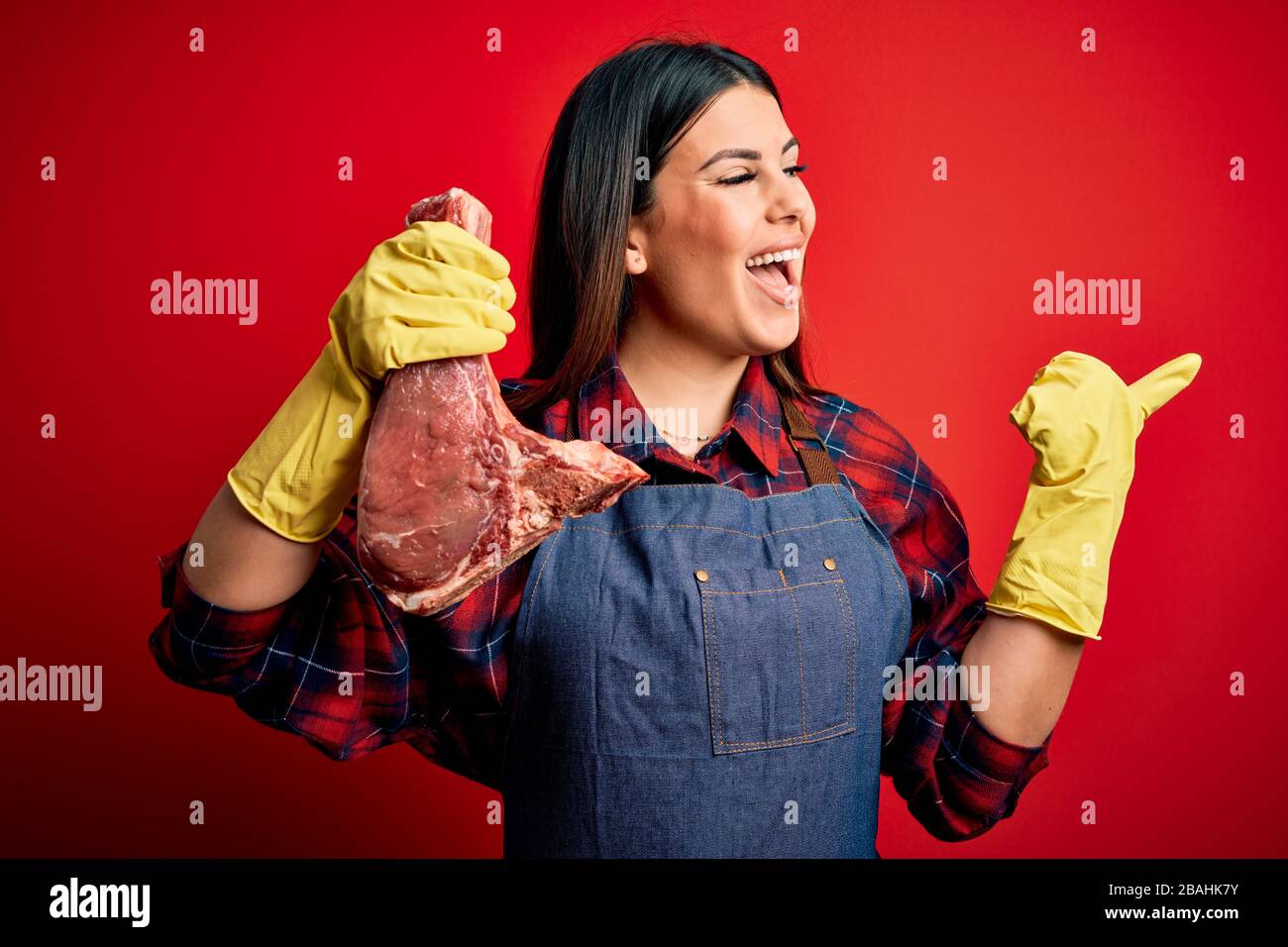 Young butcher woman holding fresh raw beef meat stake over red ...