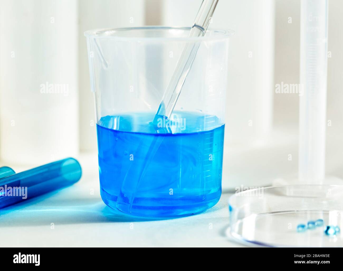 Blue liquid with a glass stir in a beaker with test tubes and a petri ...