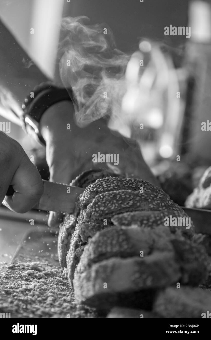 Isolated close up of a baker cutting a fresh steaming loaf of bread ...