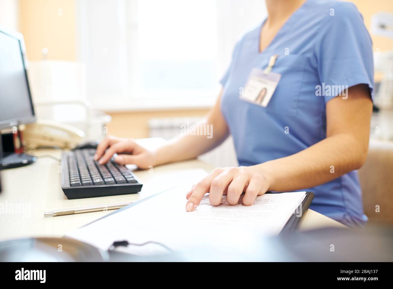 Close-up of unrecognizable nurse sitting at desk and using computer ...