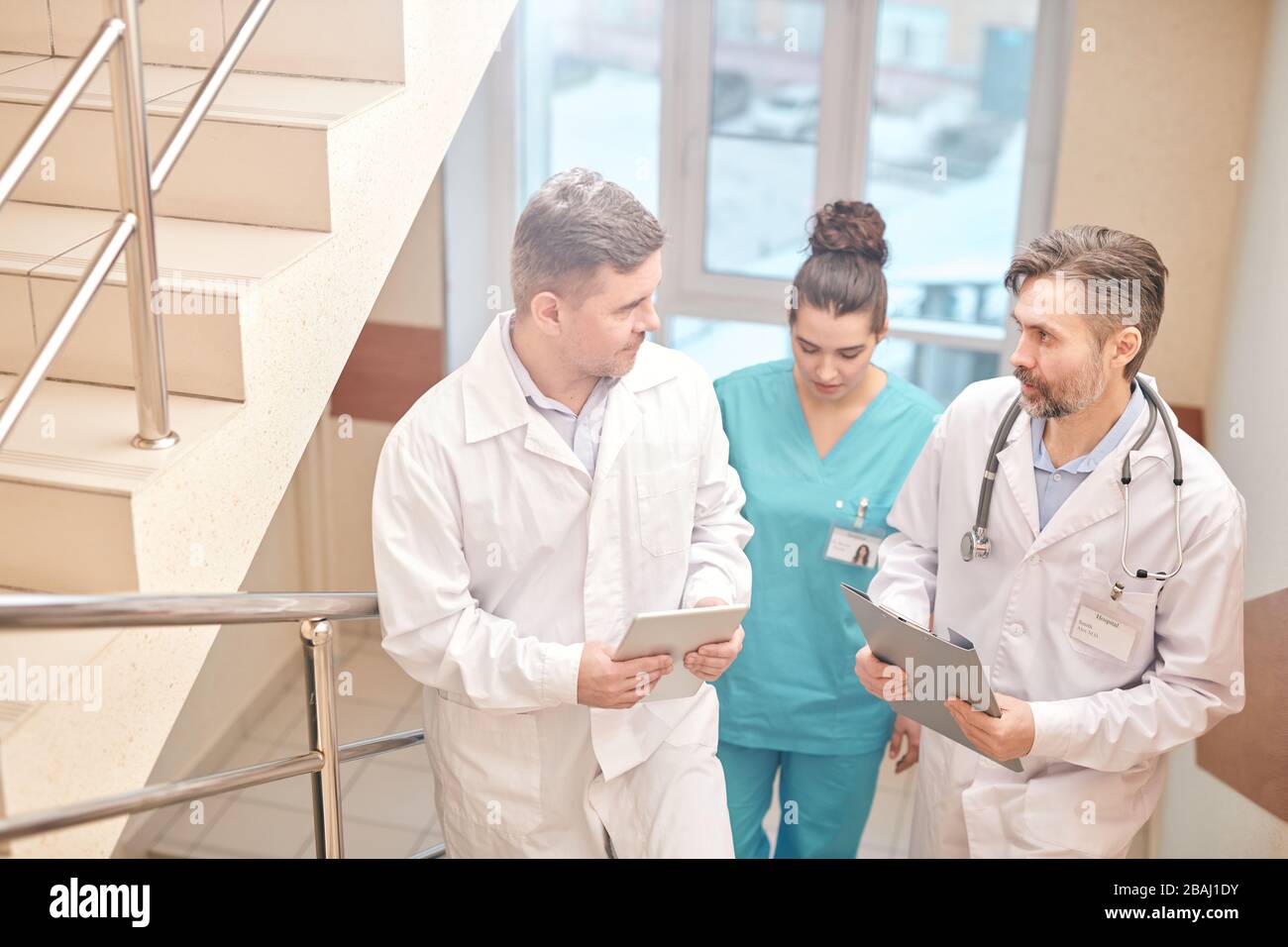 Group of doctors moving up corridor stairs and discussing coronavirus ...