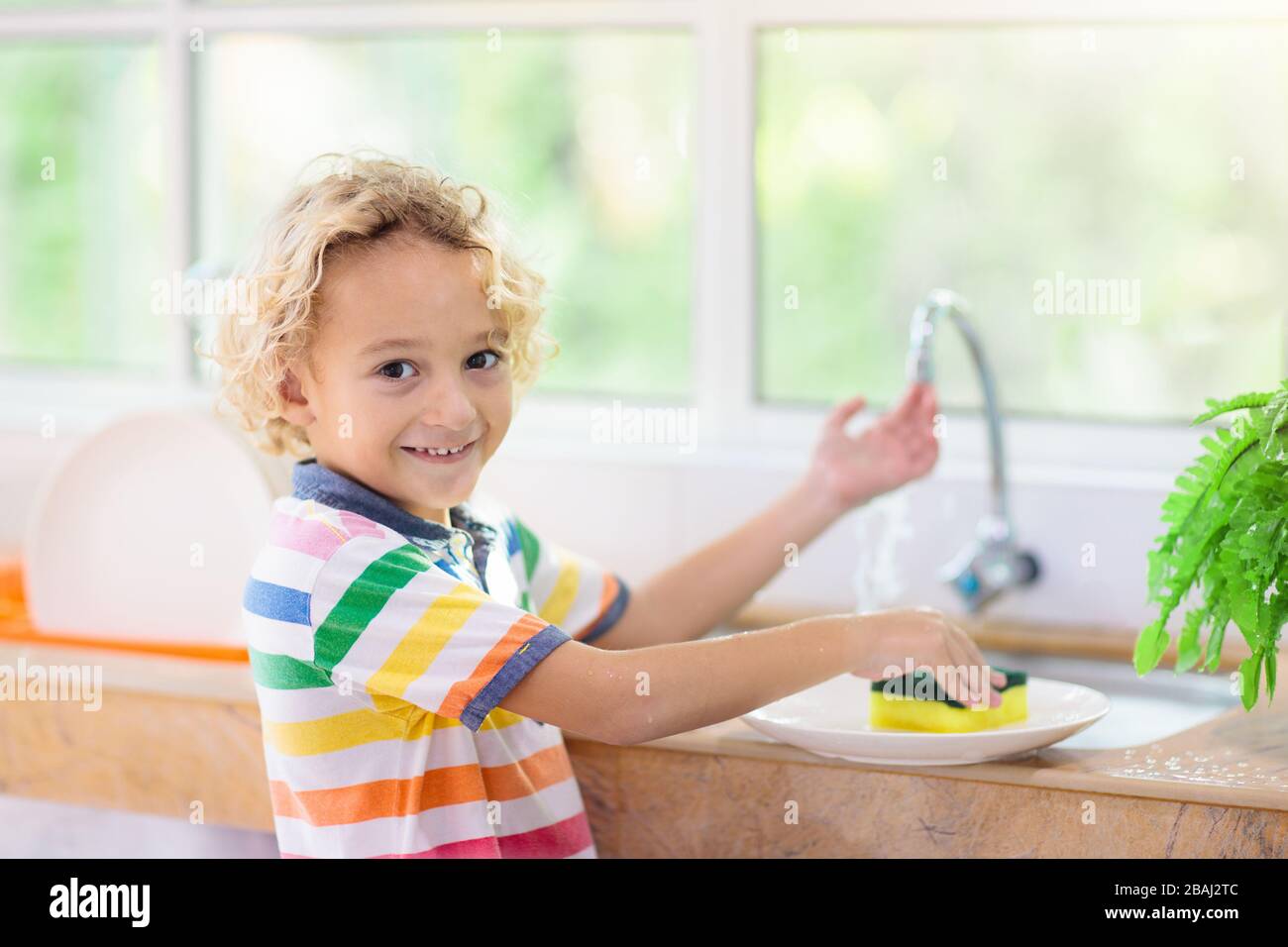 Child washing dishes. Home chores. Kid in white kitchen cleaning plates ...
