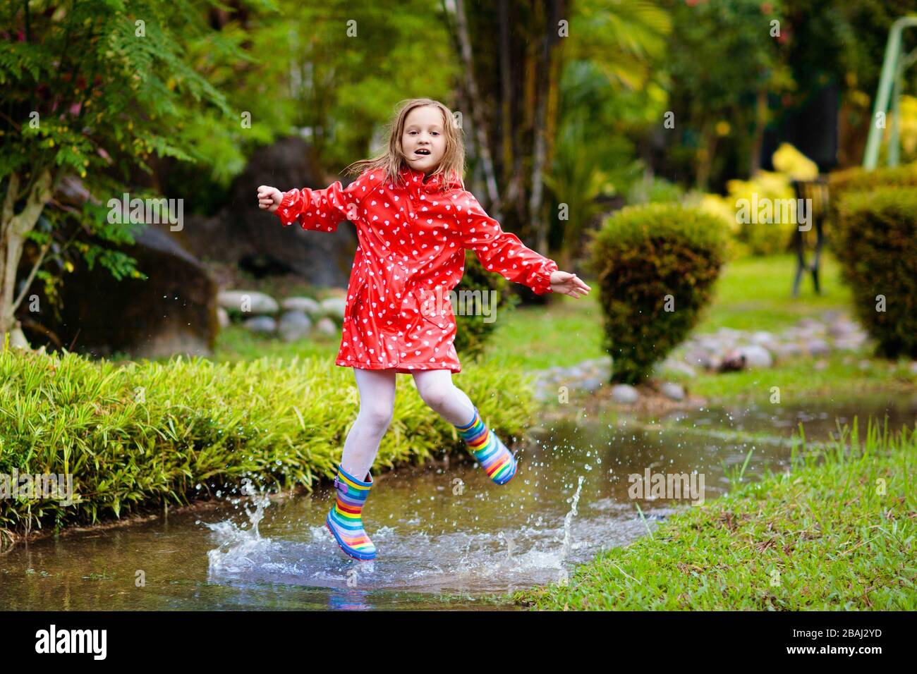 Child playing in puddle. Kids play and jump outdoor by autumn rain ...