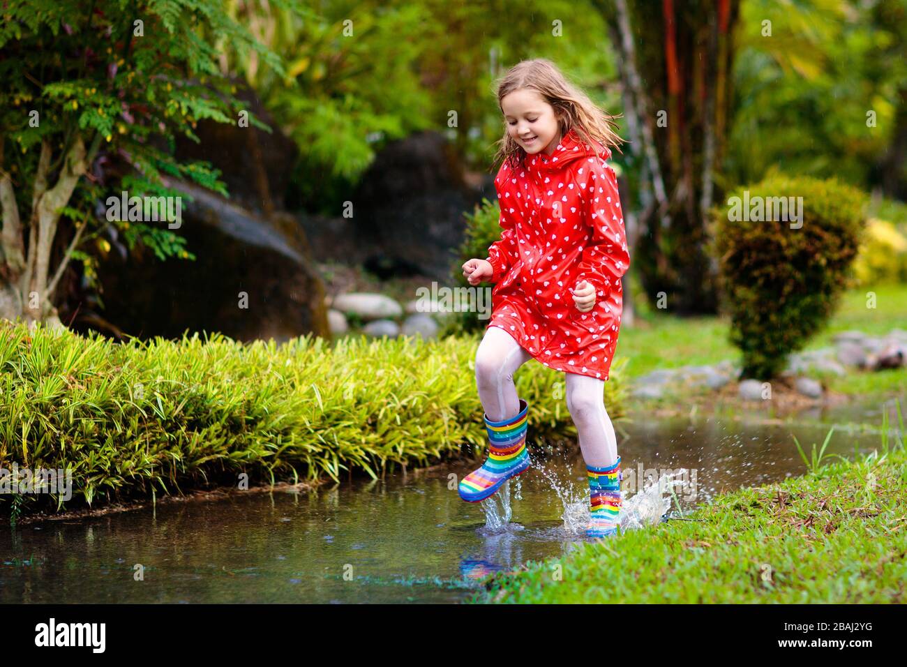 Child playing in puddle. Kids play and jump outdoor by autumn rain ...