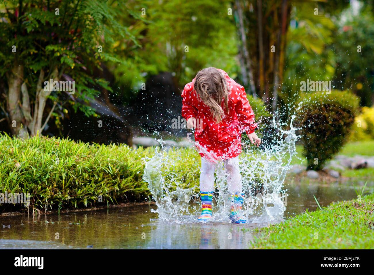 Child playing in puddle. Kids play and jump outdoor by autumn rain ...