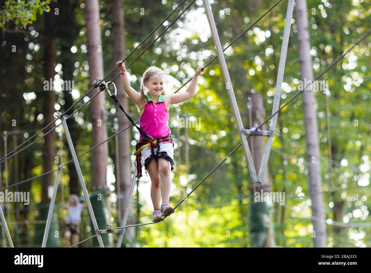Child in forest adventure park. Kids climb on high rope trail. Agility ...