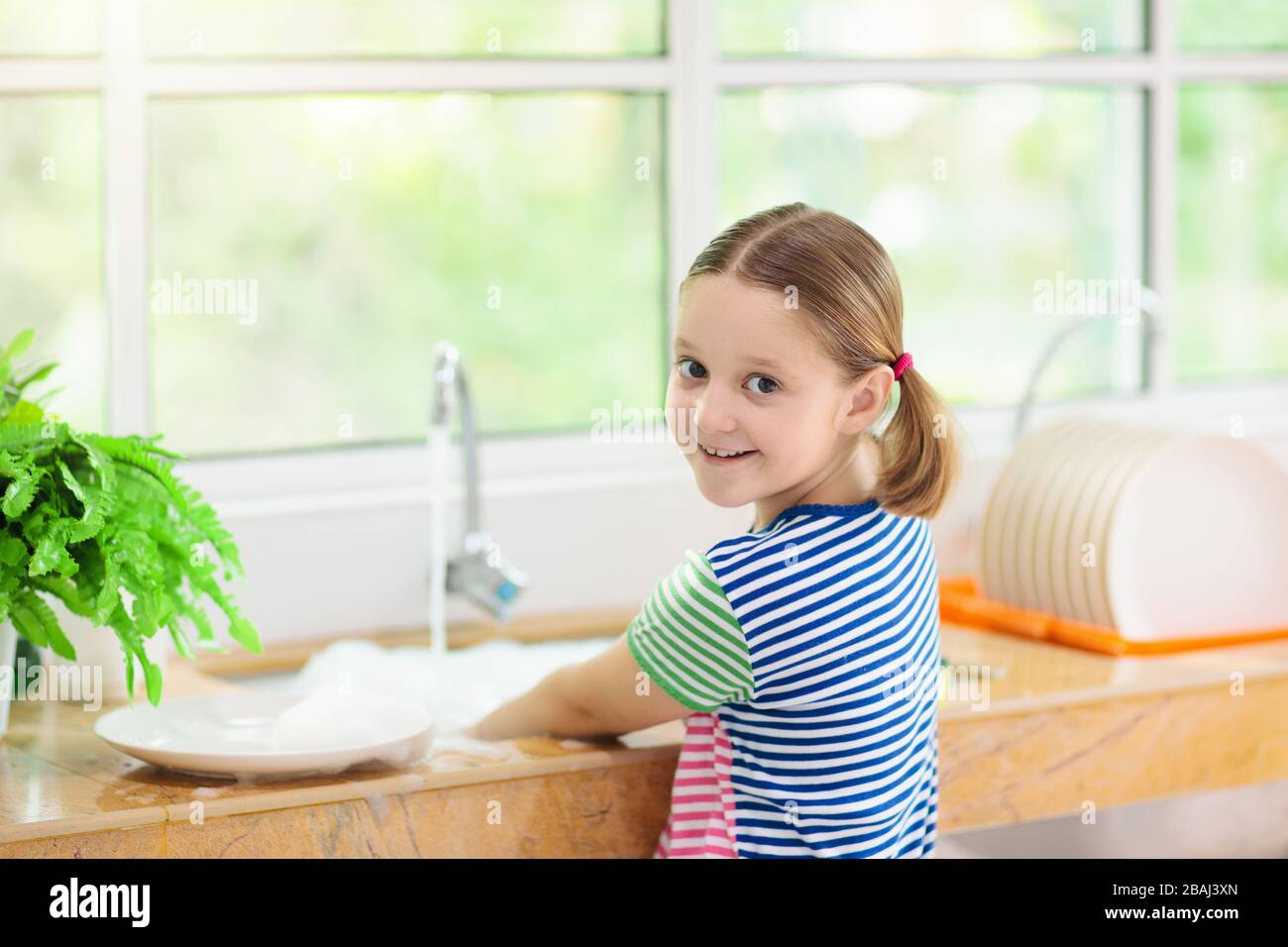 Child washing dishes. Home chores. Kid in white kitchen cleaning plates ...