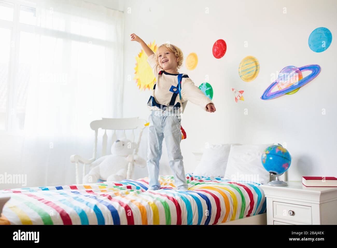 Kids play astronaut. Little boy in space costume jumping on bed with ...