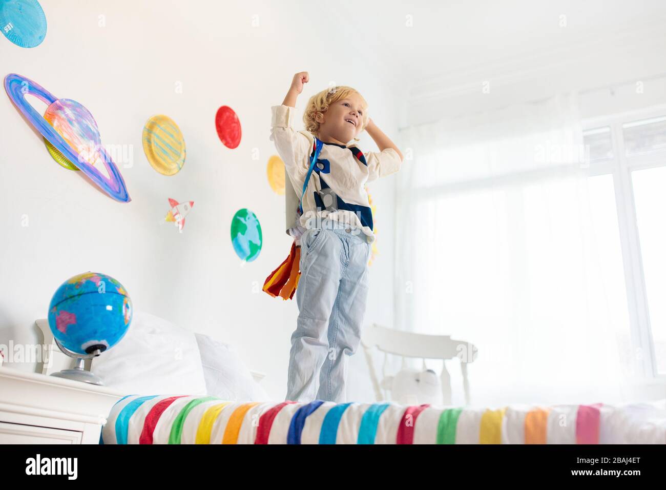 Kids play astronaut. Little boy in space costume jumping on bed with ...