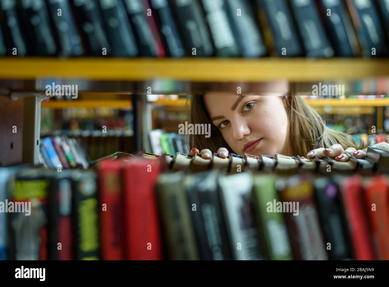 Young girl looking for book on bookshelf in library Stock Photo - Alamy