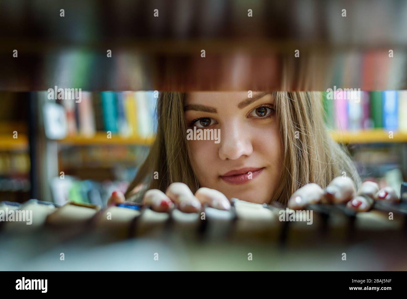 Young girl looking for book on bookshelf in library Stock Photo - Alamy