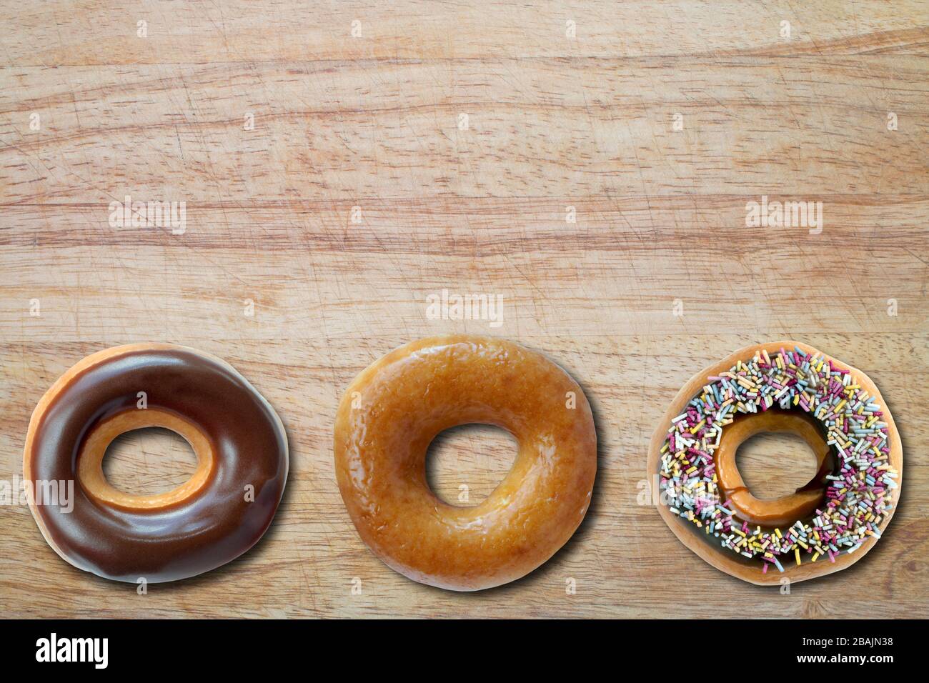 Three coated ring donuts from overhead on a chopping board with copy ...