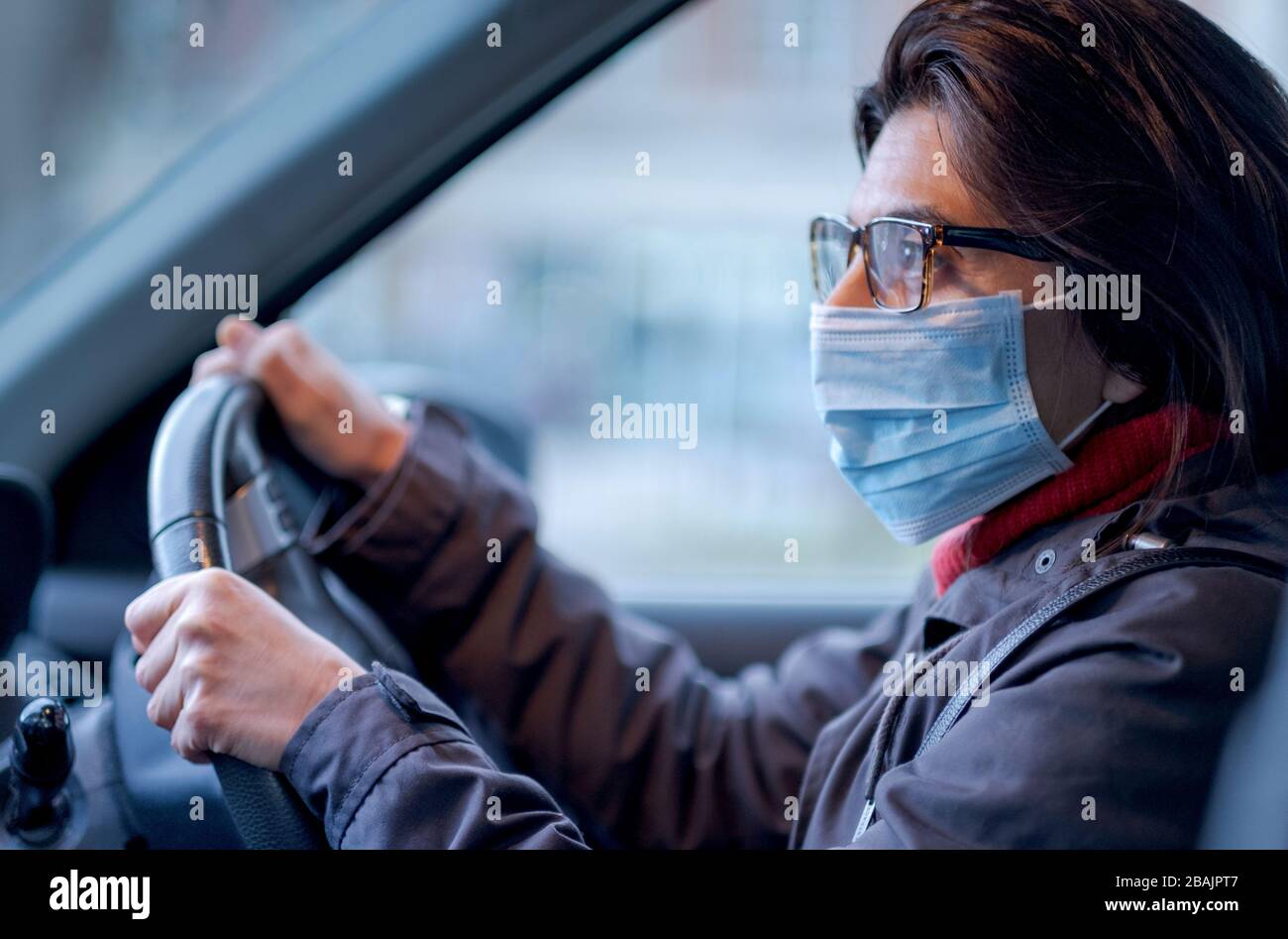 A woman driver wearing a protective face mask while driving Stock Photo ...