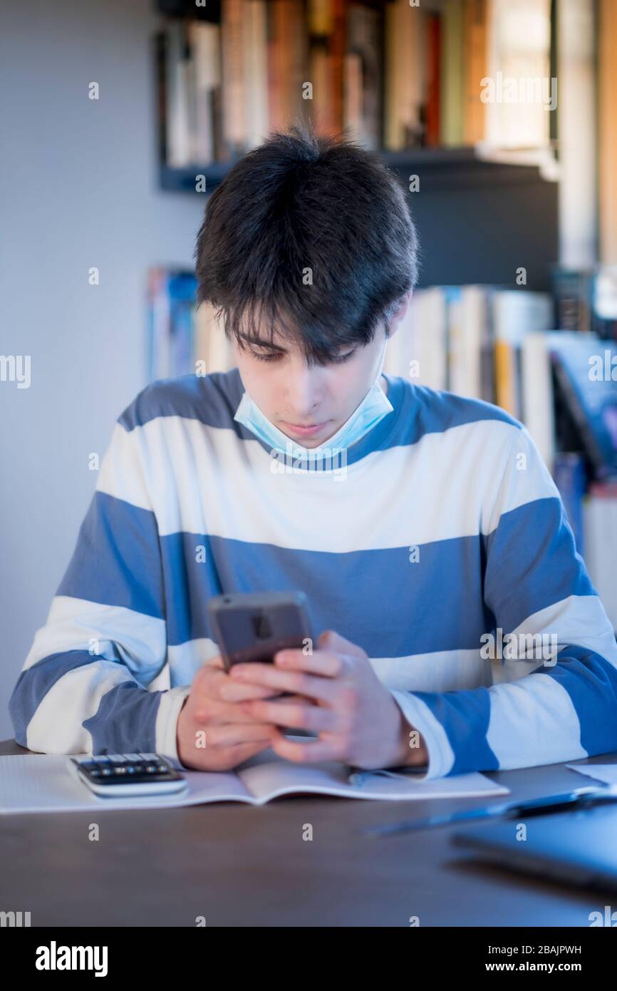 A college student wearing a mask and sending a text message to friends ...