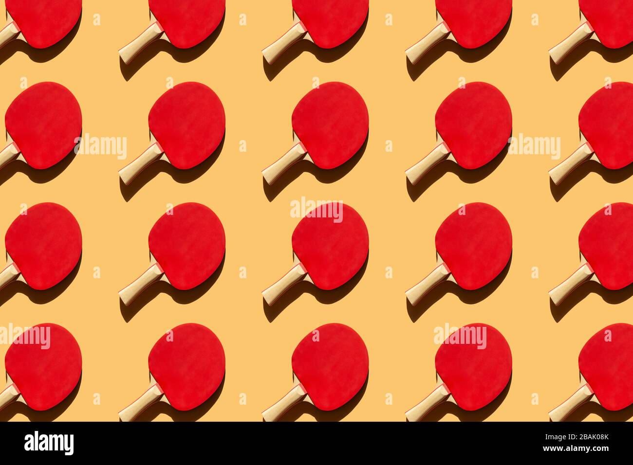 Repeating red tennis ping pong rackets with a hard shadow on a orange ...