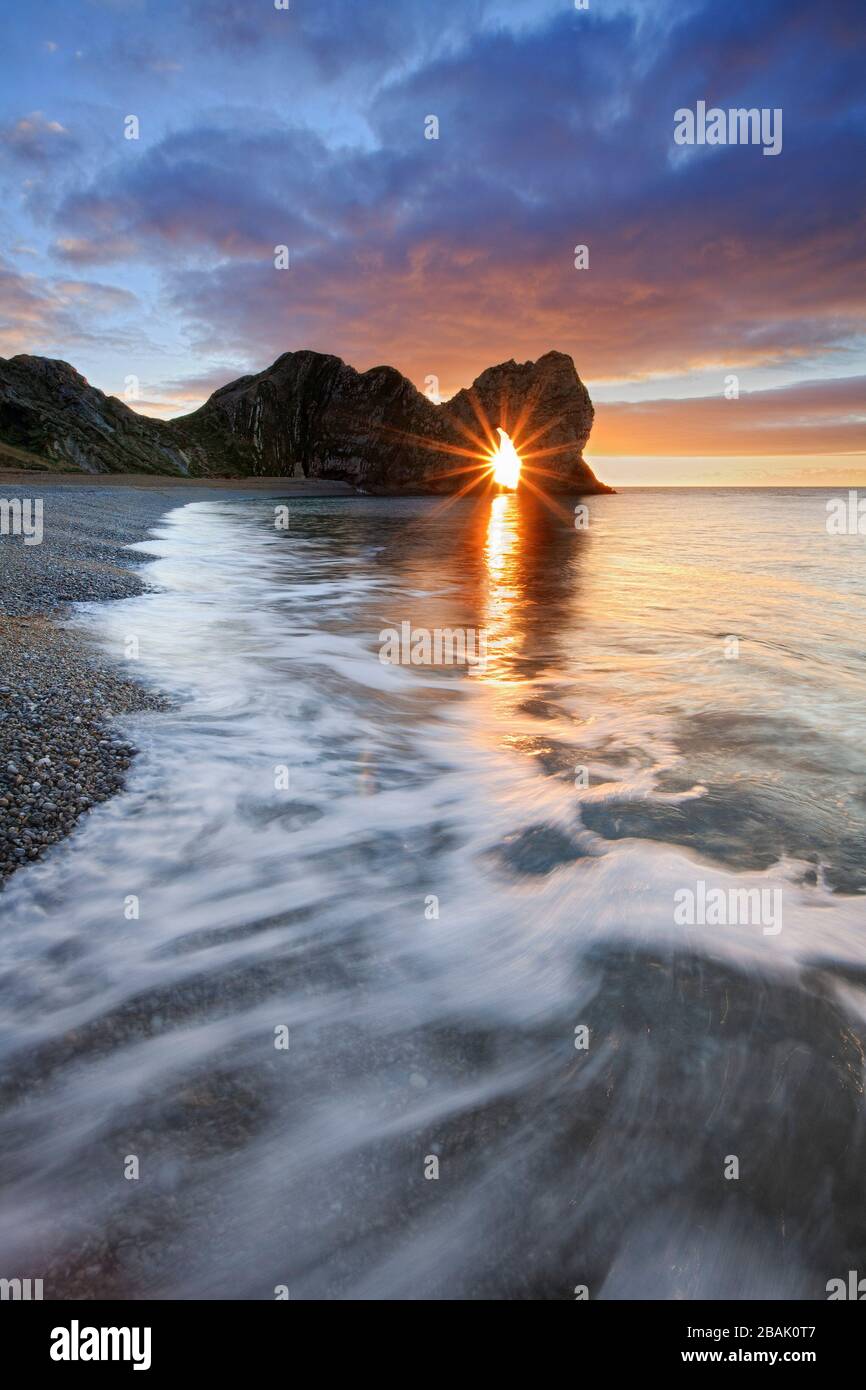 Sun shining through Durdle Door at sunrise, Jurassic Coast, Dorset ...