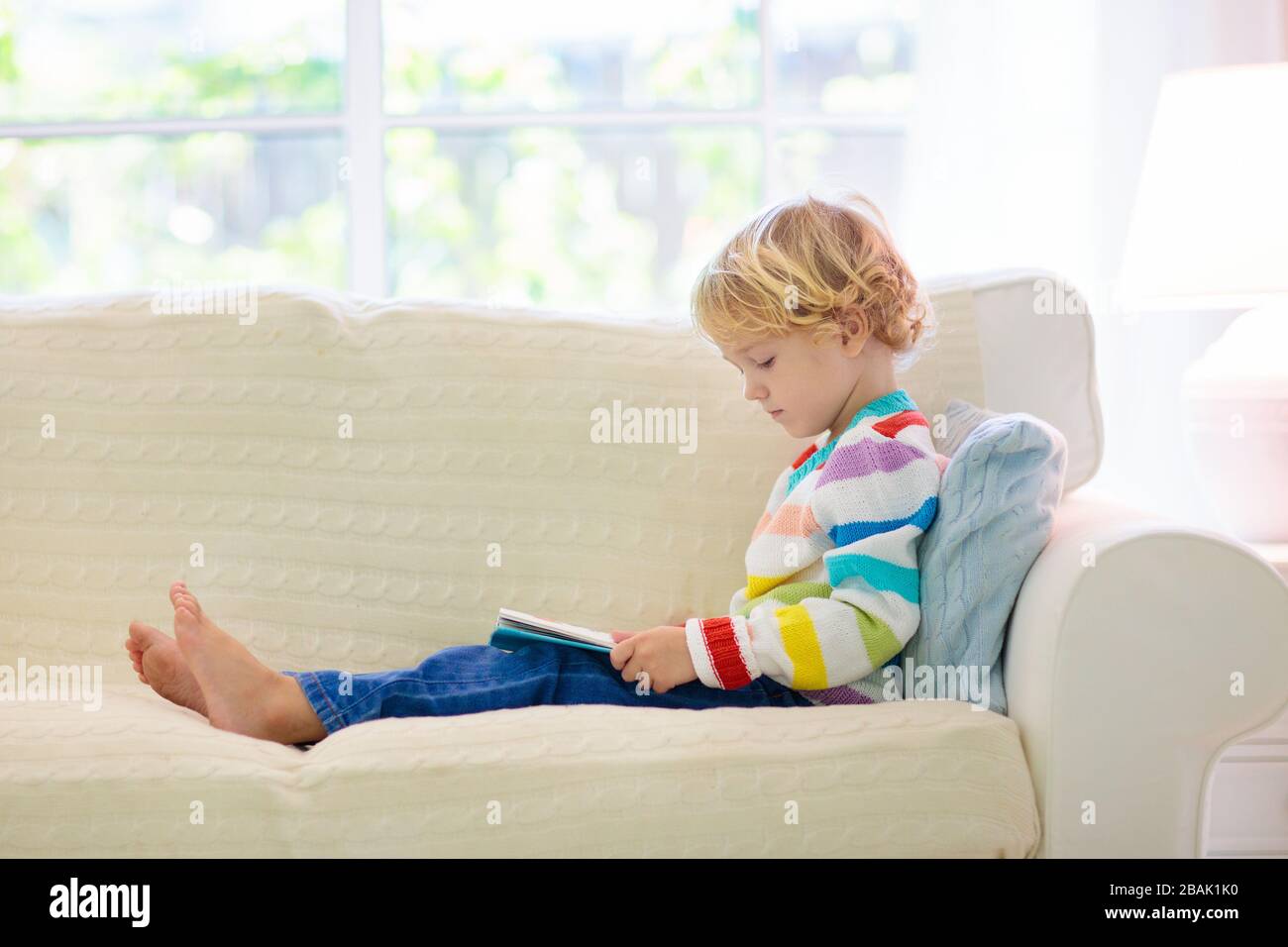 Child reading book. Kids read books. Little boy sitting on white couch ...