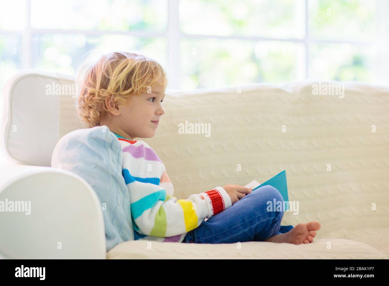 Child reading book. Kids read books. Little boy sitting on white couch ...