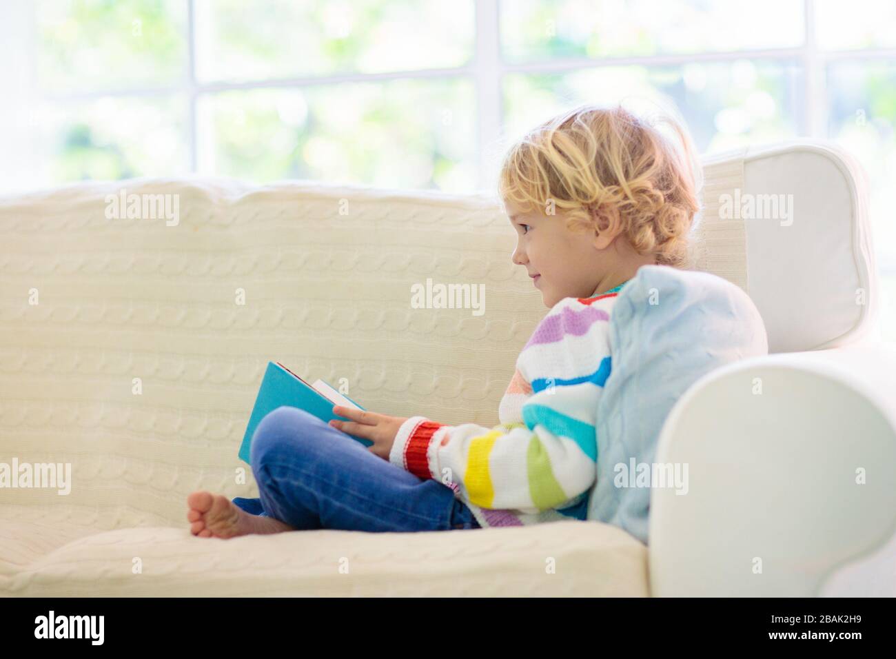 Child reading book. Kids read books. Little boy sitting on white couch ...