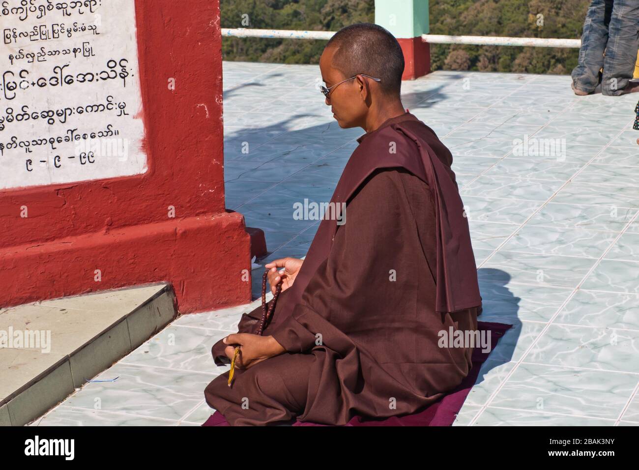 A female Buddhist nun meditating in front of a stone slab with ...