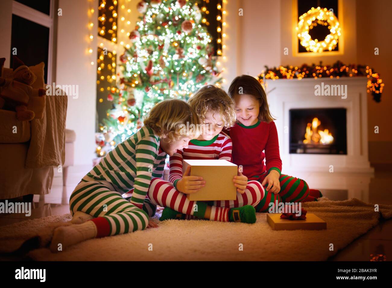 Children at Christmas tree and fireplace on Xmas eve. Family with kids ...