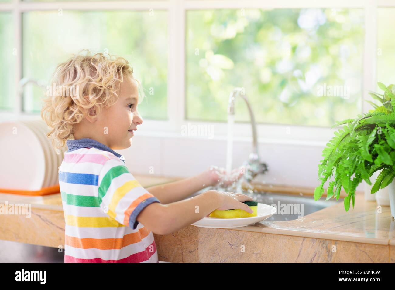 Child washing dishes. Home chores. Kid in white kitchen cleaning plates ...